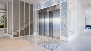 Um elevador moderno com visor digital, soalho estampado e escadas com balaústres de vidro.