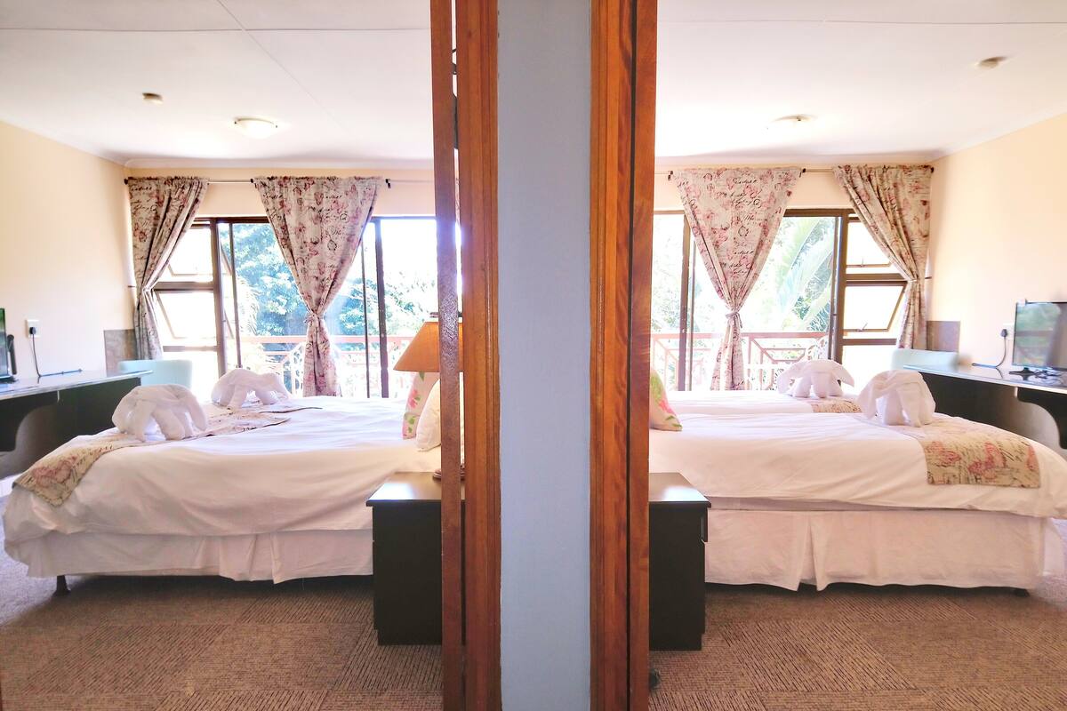 Quarto de hotel com duas camas, uma escrivaninha com computador e vista para o exterior.