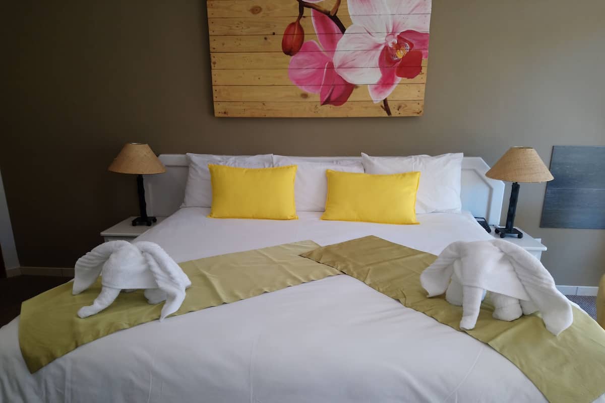 Cama bem arrumada com almofadas brancas e amarelas, um cobertor verde e duas toalhas brancas sobre a cama.