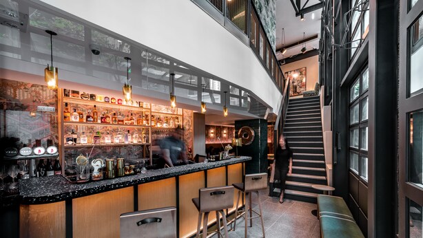 Uma área de bar com balcão alto, vários bancos e uma escada que leva a um andar superior.