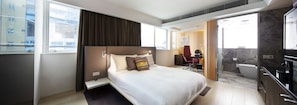 Quarto de hotel com cama, escrivaninha, cadeira, banheiro e vista para o exterior.