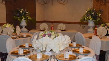 Uma sala de jantar formal com mesas redondas, toalhas brancas, pratos dourados e guardanapos brancos amarrados com fitas.