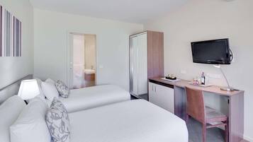 Quarto de hotel com duas camas, uma escrivaninha com cadeira, televisão e uma pequena cozinha.