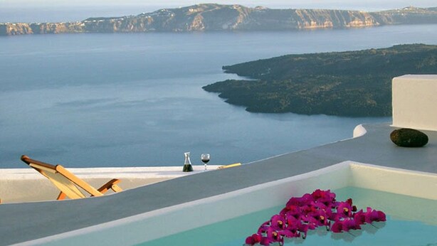 Piscina com vista para o mar e falésias, uma espreguiçadeira e uma garrafa de vinho.