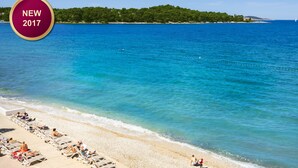 Uma praia com águas azuis cristalinas, areal dourado e uma ilha arborizada ao fundo.