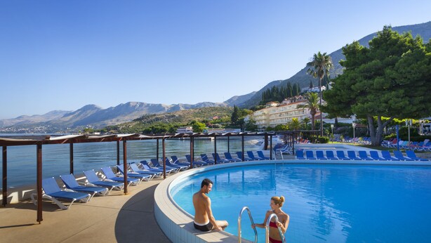 Uma área na piscina com espreguiçadeiras e vista para o mar e montanhas.