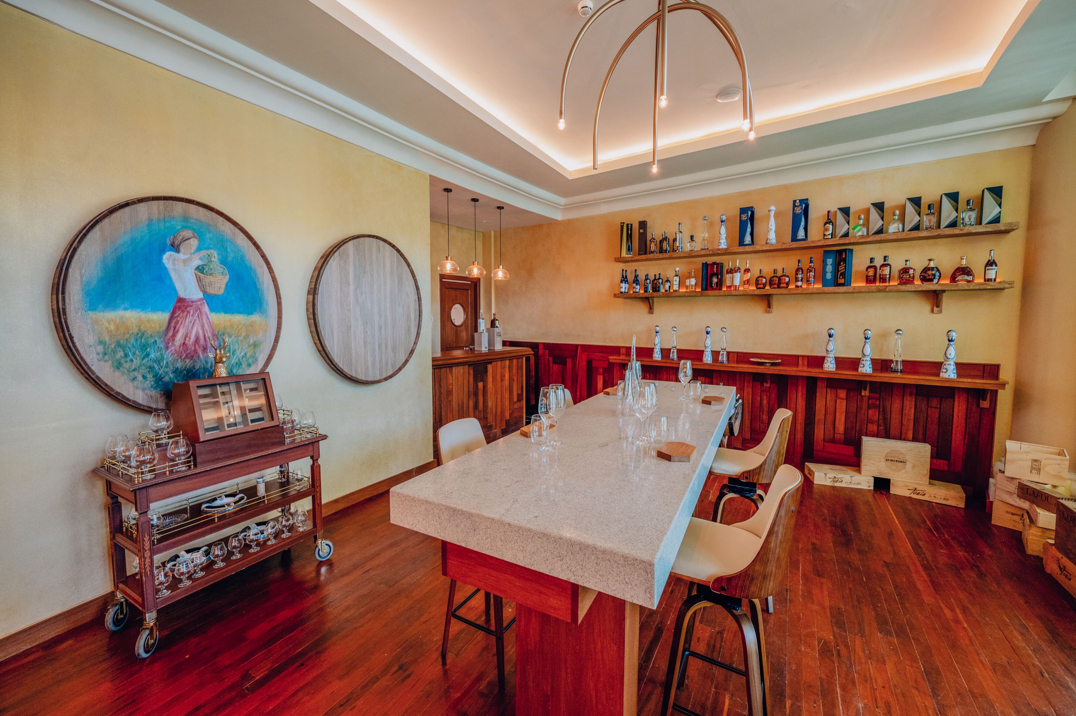 Uma área de bar com um balcão longo, vários bancos e um painel de bebidas na parede.