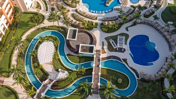 Vista aérea de um resort com várias piscinas, palmeiras e áreas de lazer.