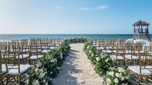 Passadeira de casamento na praia, com cadeiras e decorações florais.