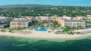 Um resort com vários edifícios, uma piscina central e uma praia.