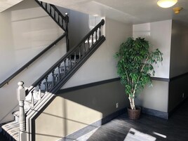 Uma escadaria com corrimão preto e balaústres brancos, que leva a um patamar com um vaso de planta.