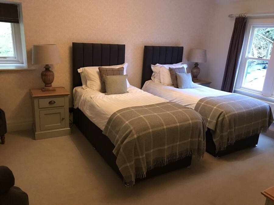 Quarto duplo com duas camas, cada uma com cabeceira, mesas de cabeceira, abajures e janela com cortinas.