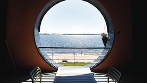 Janela circular com vista para uma praia e água.