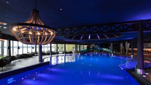 Uma grande piscina interior com design moderno, incluindo um candelabro único e vista para o exterior através de amplas janelas.