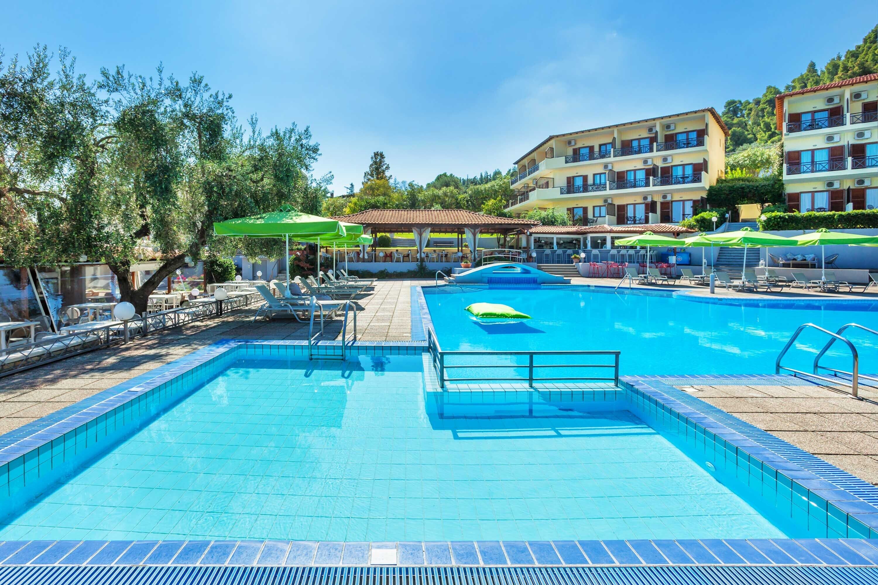 Piscina com espreguiçadeiras e guarda-sóis, cercada por edifícios com varandas.