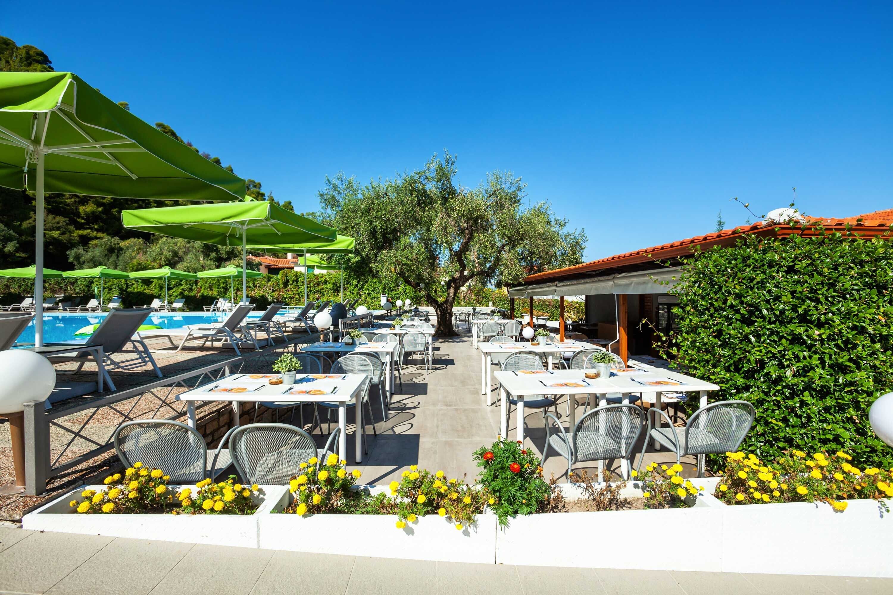 Restaurante à beira da piscina com mesas ao ar livre, guarda-sóis e vista para a piscina.