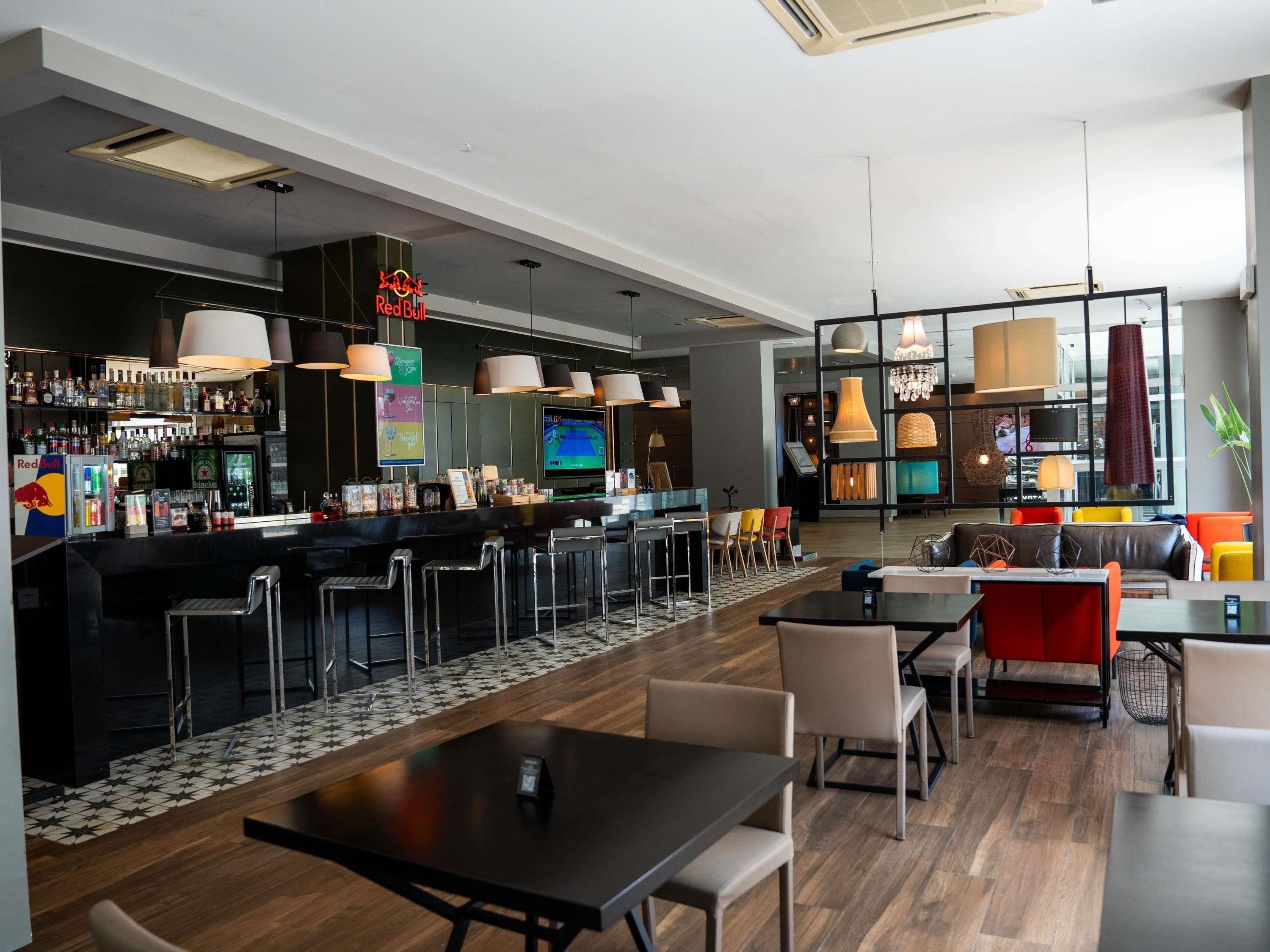 Uma área de bar moderna com um letreiro da Red Bull, uma tela de televisão e diversas opções de assento, incluindo banquetas e mesas.