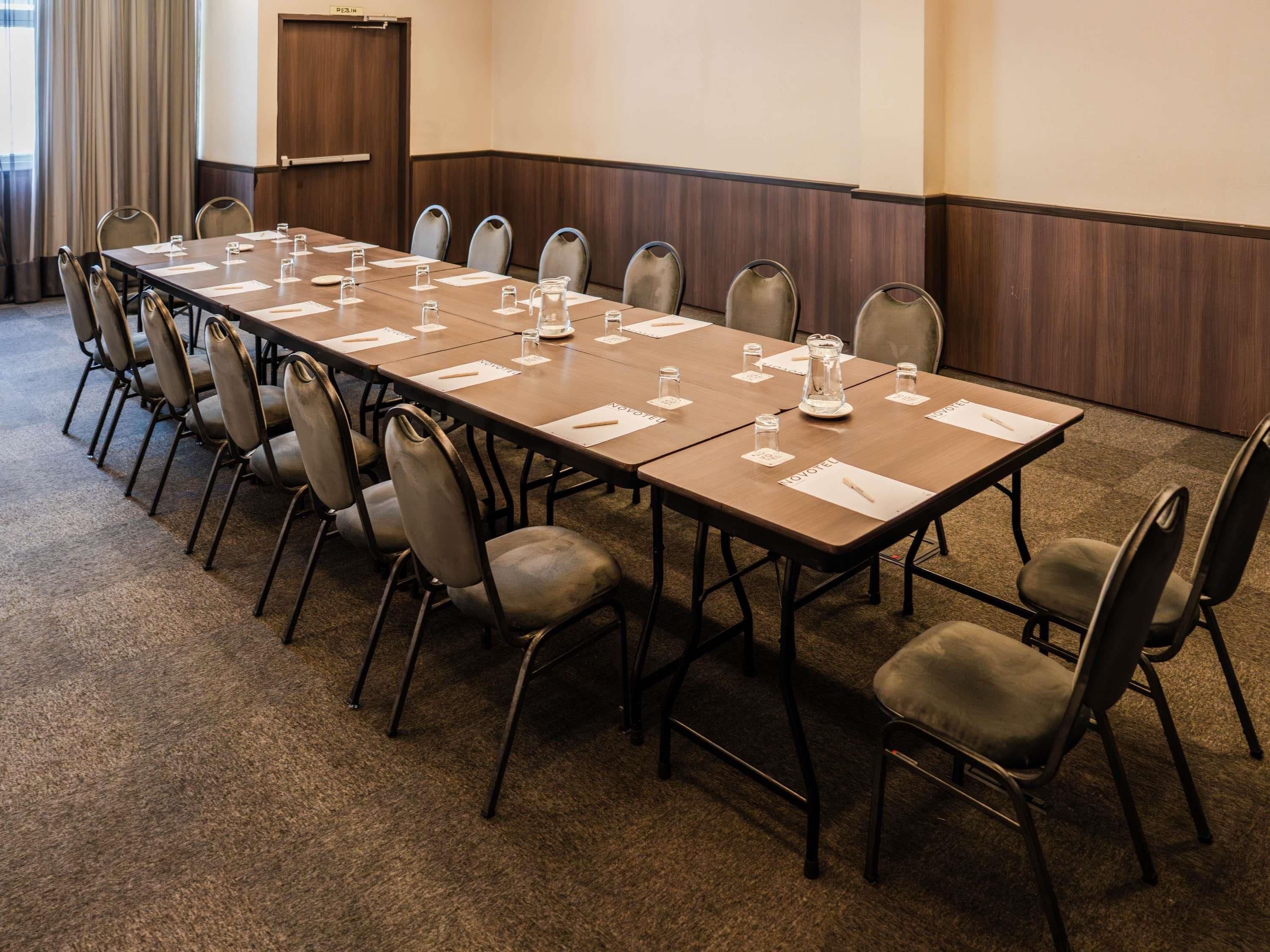 Uma sala de conferência com uma mesa comprida, cadeiras, cartões de identificação e um jarro de água.