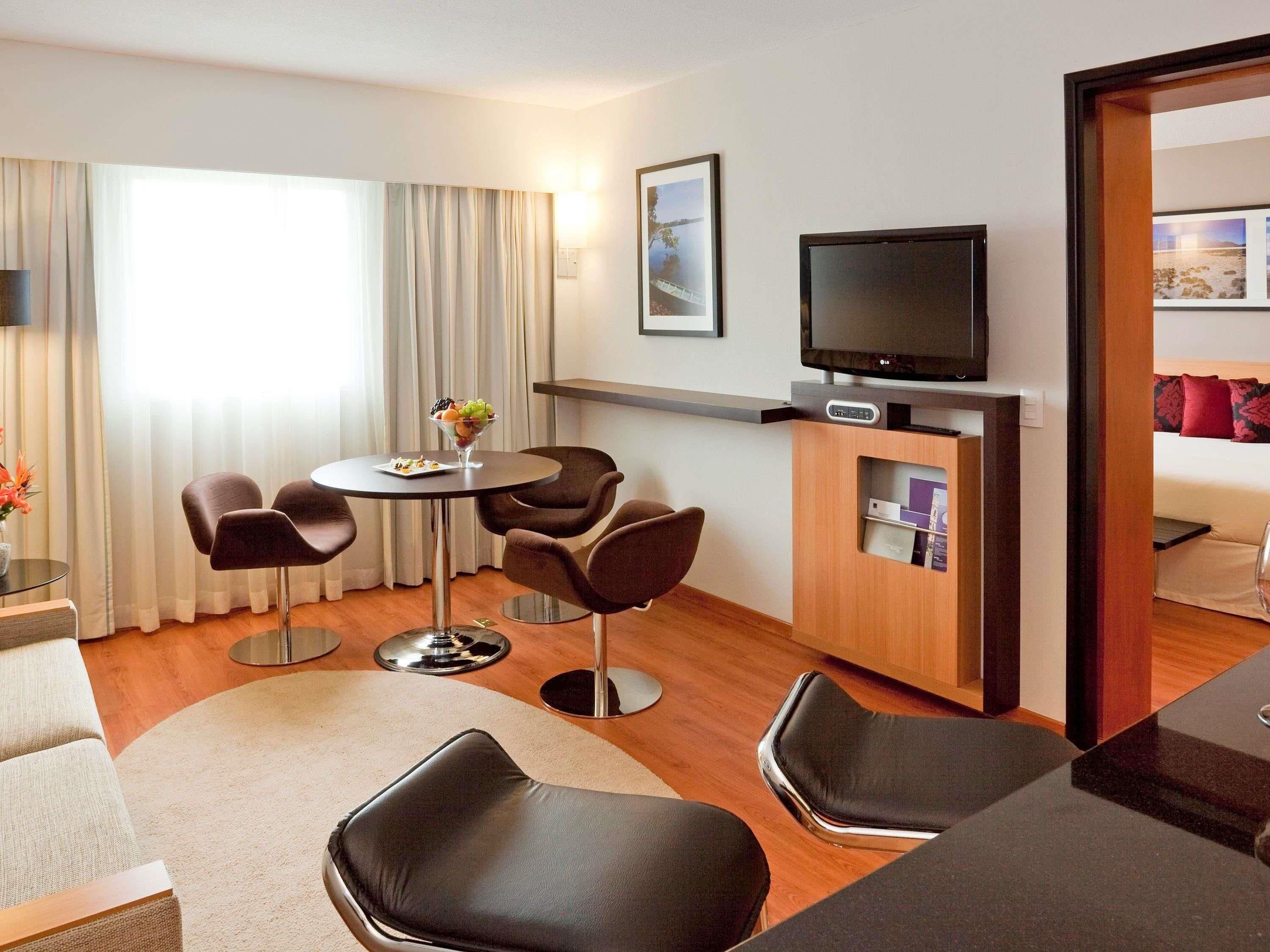 Quarto de hotel com área de refeições, televisão e cama.