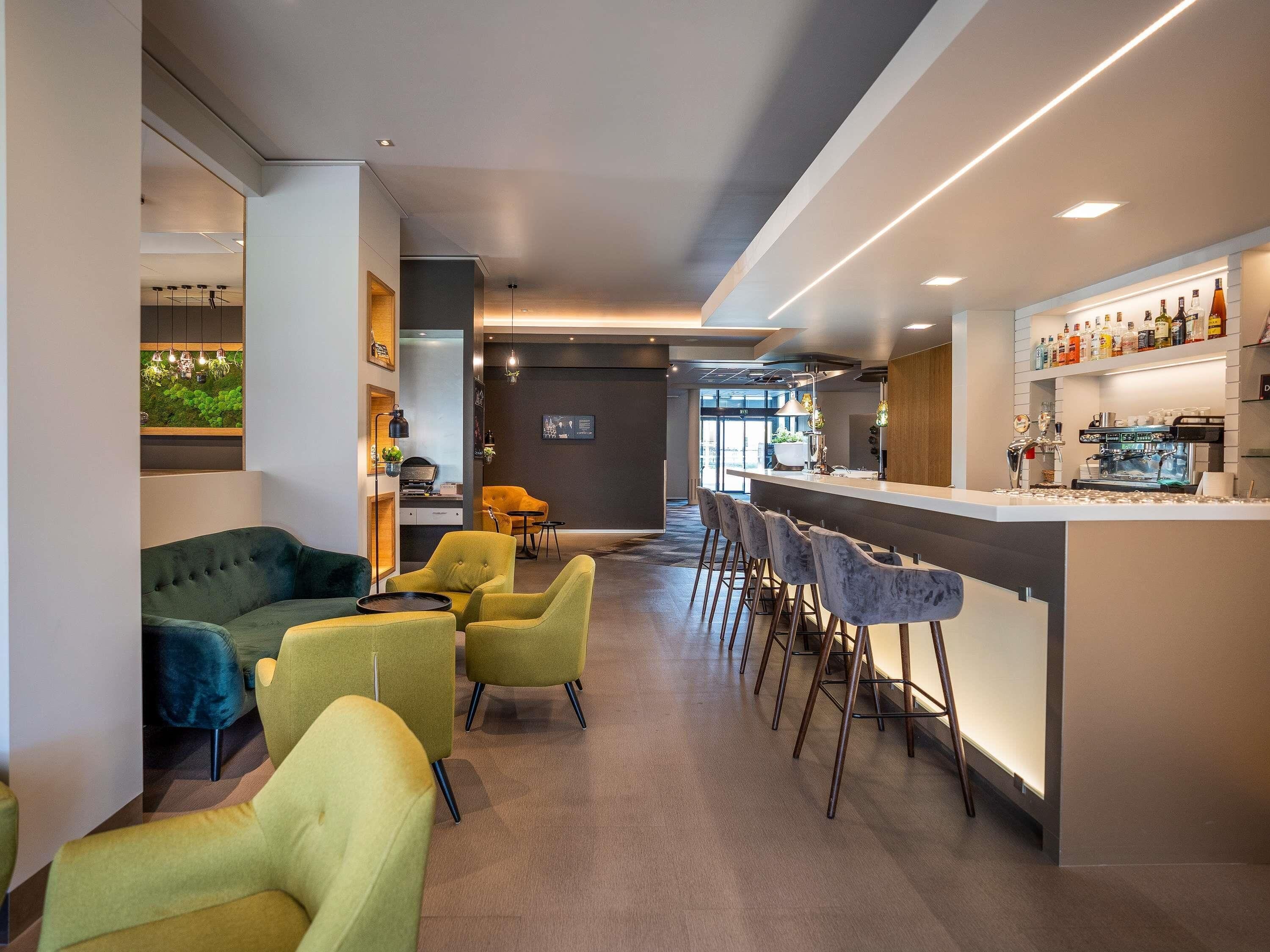 Uma área de bar moderna, com balcão, banquetas e um espaço com cadeiras.