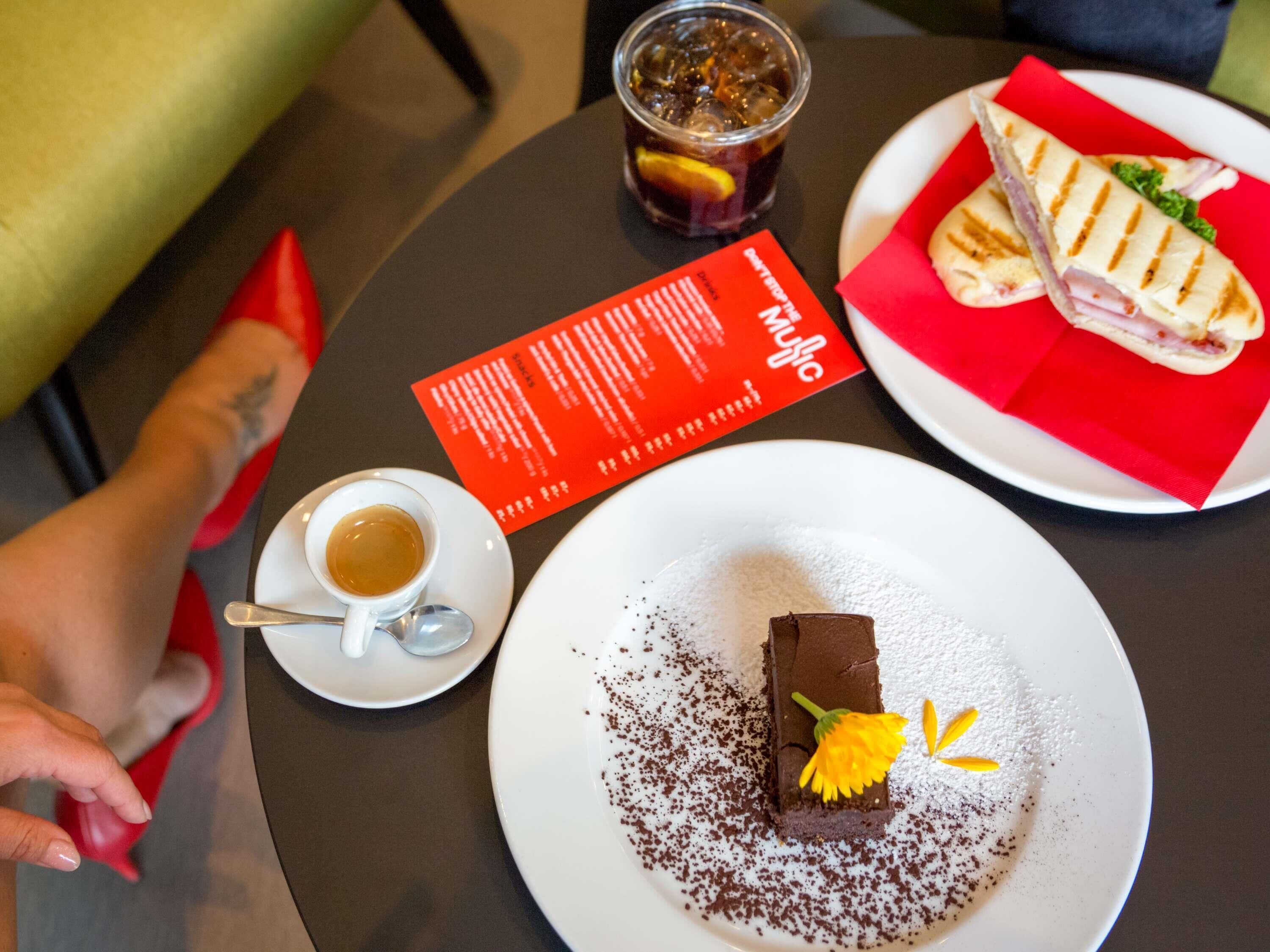 Um prato com sobremesa, um pedaço de chocolate, uma chávena de café, um sanduíche e um menu sobre a mesa.