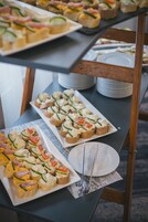Uma mesa de buffet com diversos alimentos, incluindo sanduíches e petiscos, dispostos em pratos e bandejas.