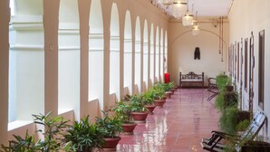 Um corredor com janelas arqueadas, plantas em vasos e lustres.
