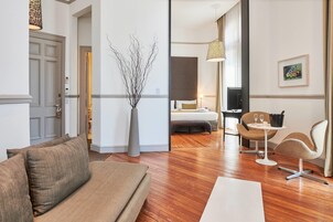 Quarto de hotel moderno com piso de madeira, um sofá, uma cama, uma escrivaninha e uma cadeira.