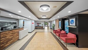 Uma área de recepção de hotel com um balcão de madeira, espaço para sentar com cadeiras vermelhas e um design de teto moderno.