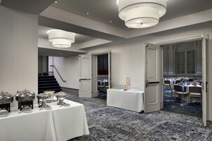 Um hall de hotel com um espaço para buffet, uma escadaria e uma área de refeições com mesas e cadeiras.