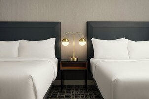 Quarto de hotel com duas camas, uma mesa de cabeceira com abajur e chão estampado.