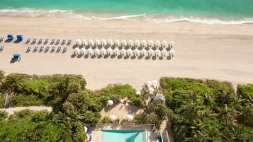 Vista aérea de um resort à beira-mar, com fileiras de espreguiçadeiras, piscina e vegetação exuberante.
