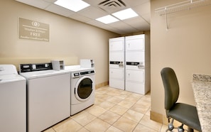 Uma lavanderia de hotel com máquina de lavar e secadora Maytag, área para dobrar roupas e uma cadeira.