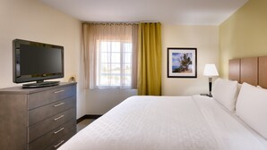 Quarto de hotel com cama, televisão em uma cômoda, janela com cortinas, quadro pendurado na parede e abajur.