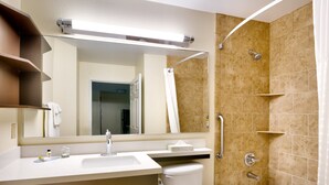 Uma casa de banho moderna com lavatório, sanita e banheira. Inclui cortina de chuveiro, espelho e um prateleira com produtos de higiene pessoal.