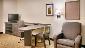 Quarto de hotel com escrivaninha, cadeira, televisão, telefone e quadro na parede.