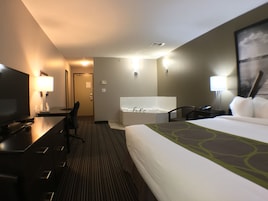 Quarto de hotel com uma cama, uma escrivaninha com televisão, uma cadeira, uma banheira e uma mesa de cabeceira com abajur.