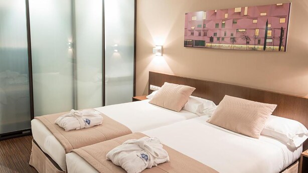 Quarto de hotel com duas camas, uma janela grande, um quadro na parede e um roupão sobre a cama.