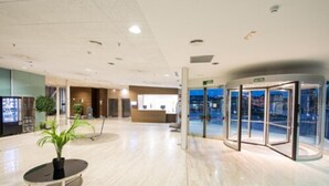 Um hall amplo com piso de mármore, balcão de recepção, porta de vidro e um vaso de planta.