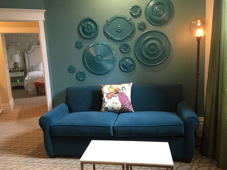 Um sofá azul com um travesseiro colorido, uma mesa de centro branca e pratos decorativos na parede.