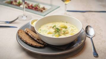 Uma tigela de sopa com pão e uma colher num prato, com um copo de vinho branco e um garfo ao fundo.