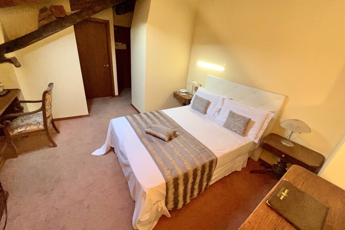 Um quarto aconchegante com cama, mesa de cabeceira, abajur e uma cadeira.