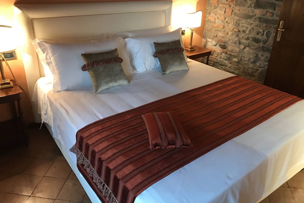 Uma cama bem arrumada com um cobertor listrado e dois travesseiros, uma parede de pedra e uma porta de madeira.