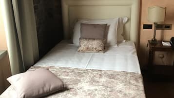 Cama bem arrumada com colcha estampada, travesseiro e cabeceira, tudo com uma parede de tijolos ao fundo.