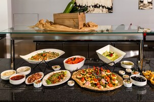 Uma mesa de buffet com diversos pratos, incluindo saladas, aperitivos e uma grande travessa de comida.