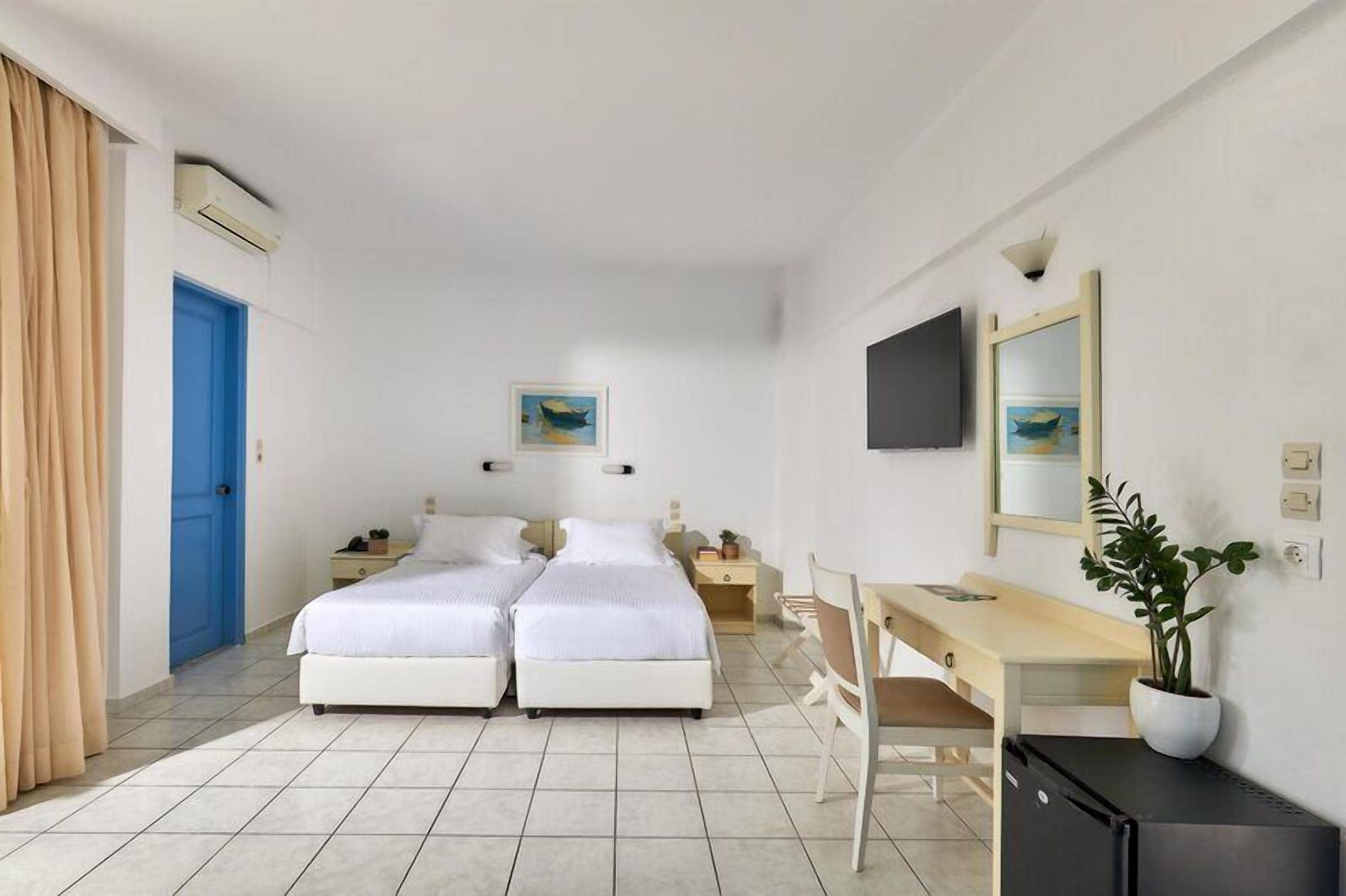 Quarto de hotel com duas camas, uma escrivaninha, uma cadeira, televisão, espelho e uma planta.