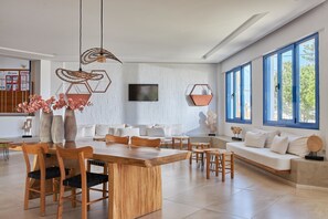 Uma sala de estar moderna com uma mesa de jantar de madeira, sofás e uma televisão fixada na parede.