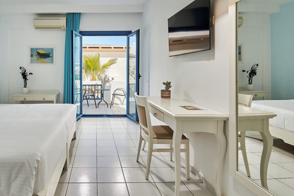 Quarto de hotel com cama, escrivaninha, cadeira e varanda com vista.