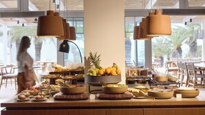 Buffet com diversos tipos de comida e uma mulher andando ao fundo.