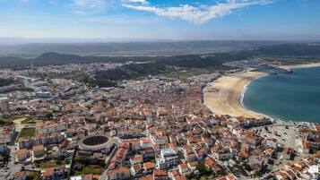 Vista aérea de uma cidade costeira com praia, área residencial densa e um edifício redondo em destaque.